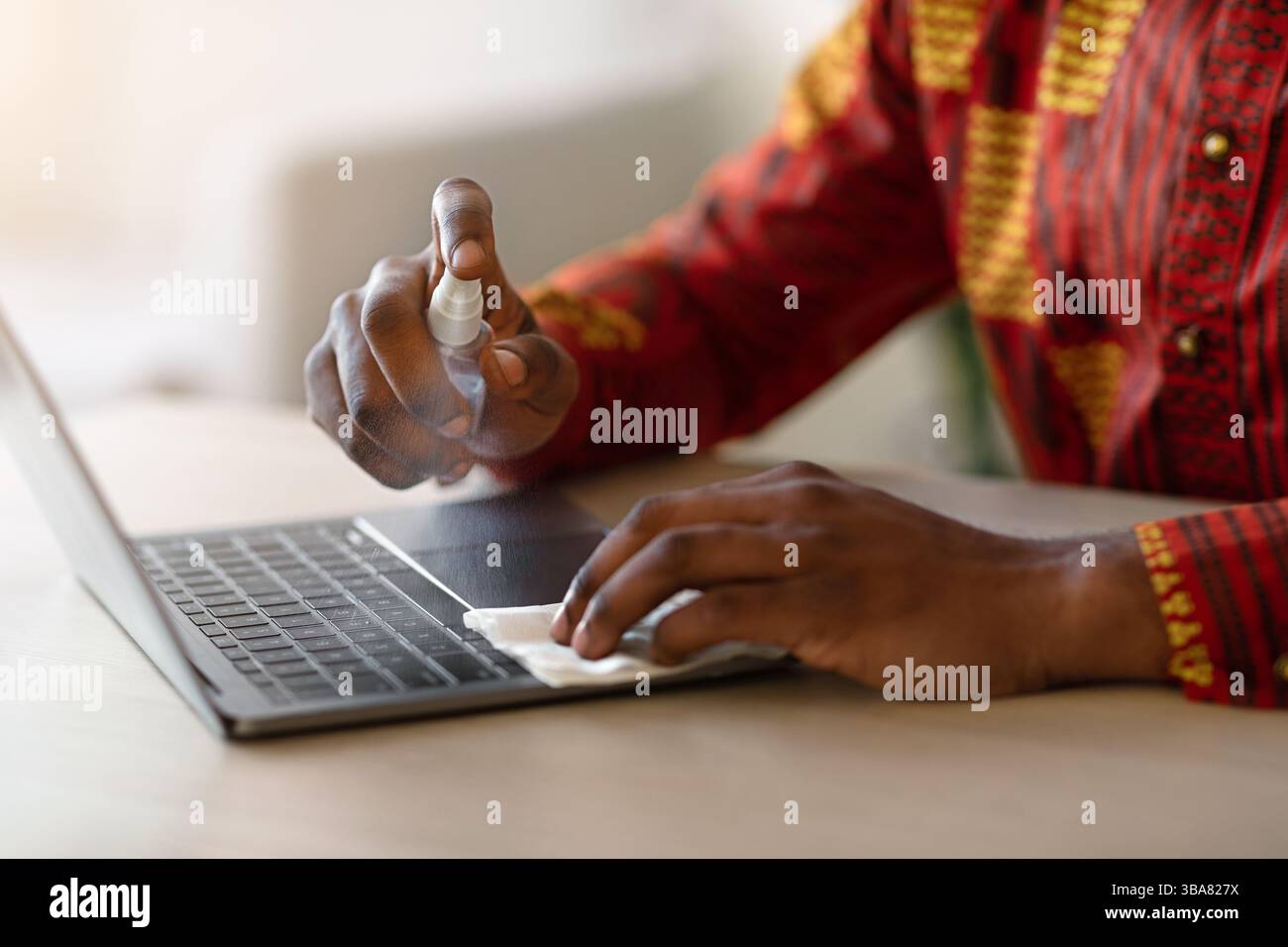 Unrecognizable african man sanitizing laptop keyboard surface with ...