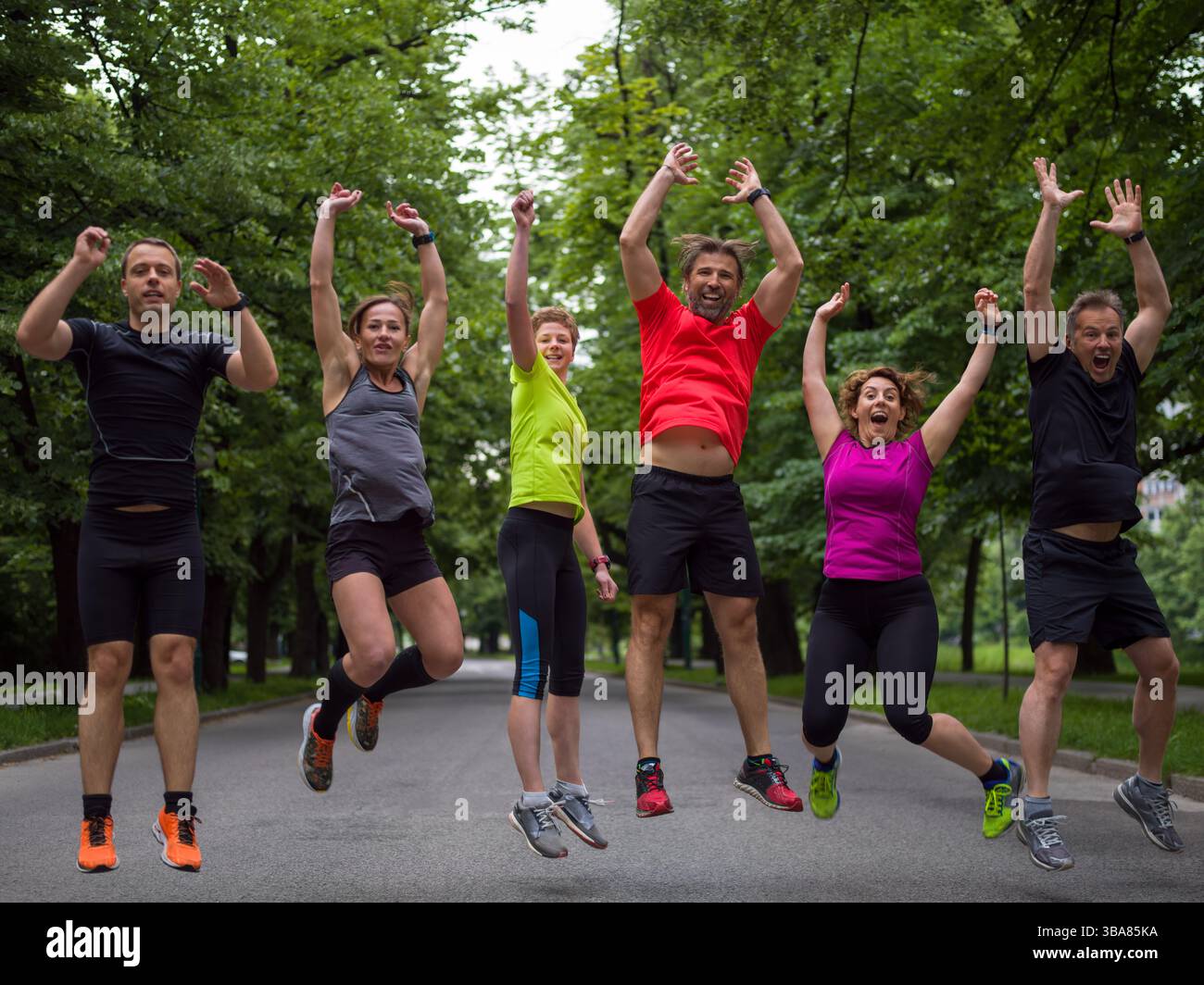group of healthy runners team jumping in the air at city park during ...