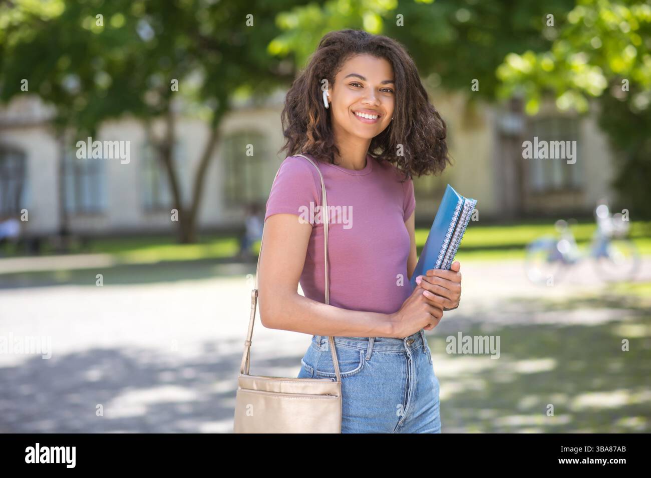 Smiling African American female student holding notebooks standing near ...