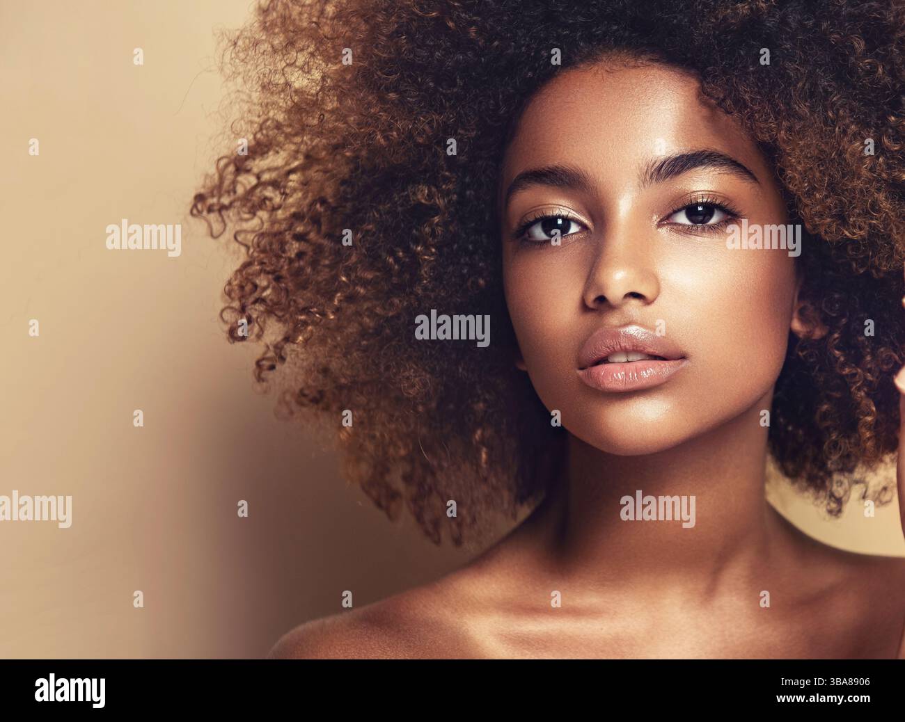 Mixed race woman with curly afro standing in front of beige background ...