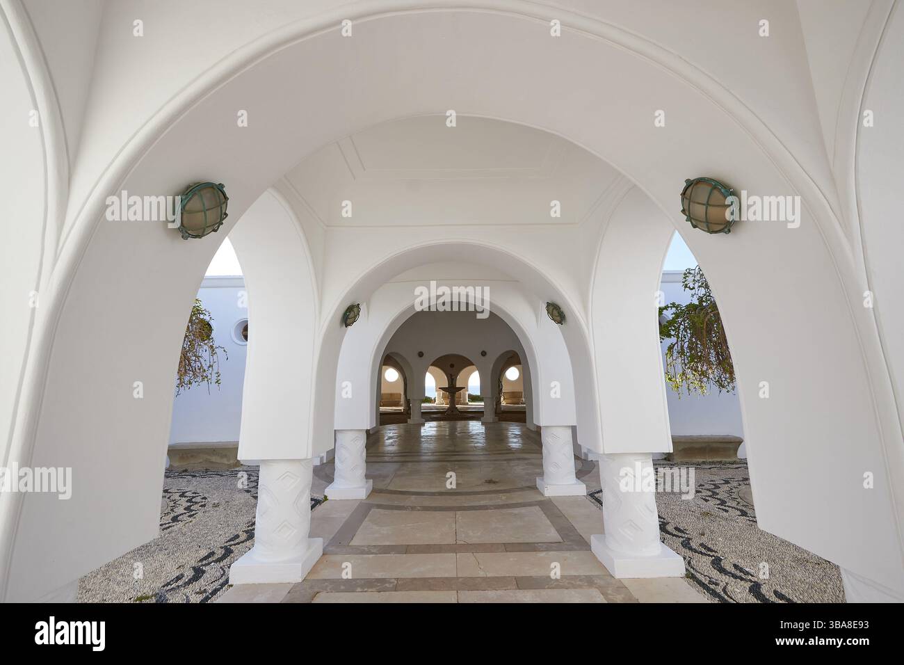 A bright corridor with white arches and decorative floor mosaic ...
