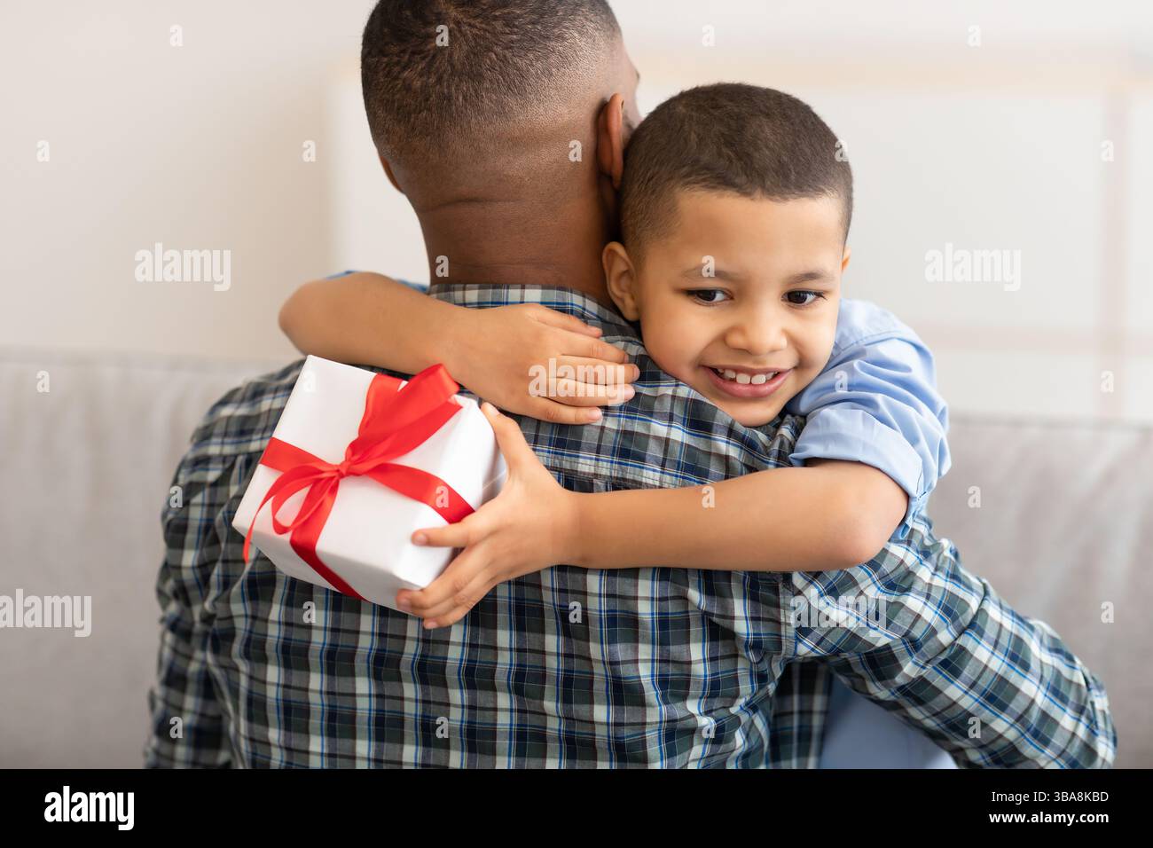 Black boy hugging his father after receiving gift box while sitting on ...