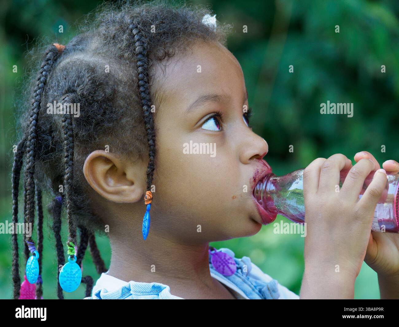 Side view of Black little girl with braids drinking juice from the ...