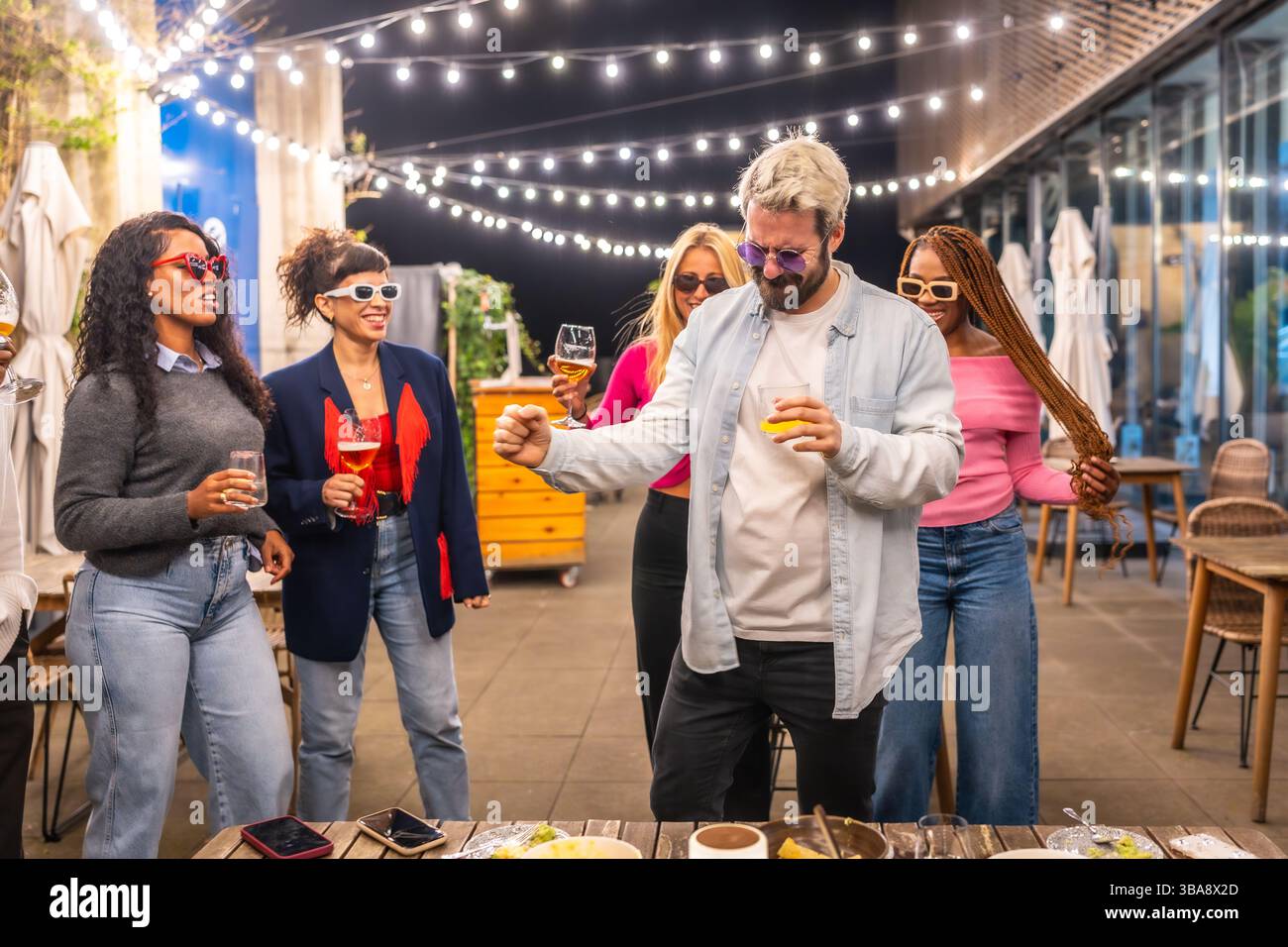 Diverse group of friends drinking and dancing together on rooftop bar ...