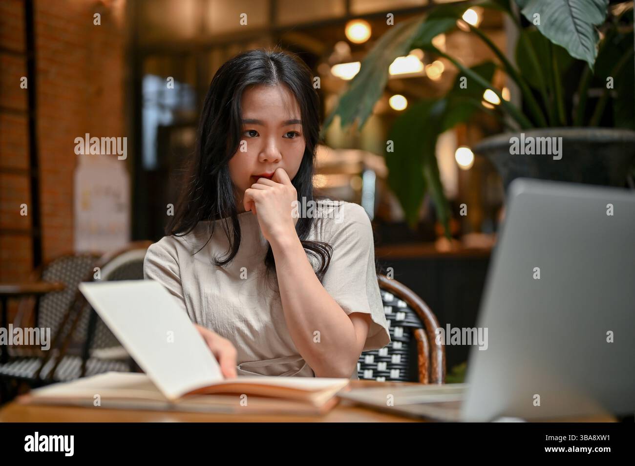 A doubtful and thoughtful young Asian woman is looking at her laptop ...