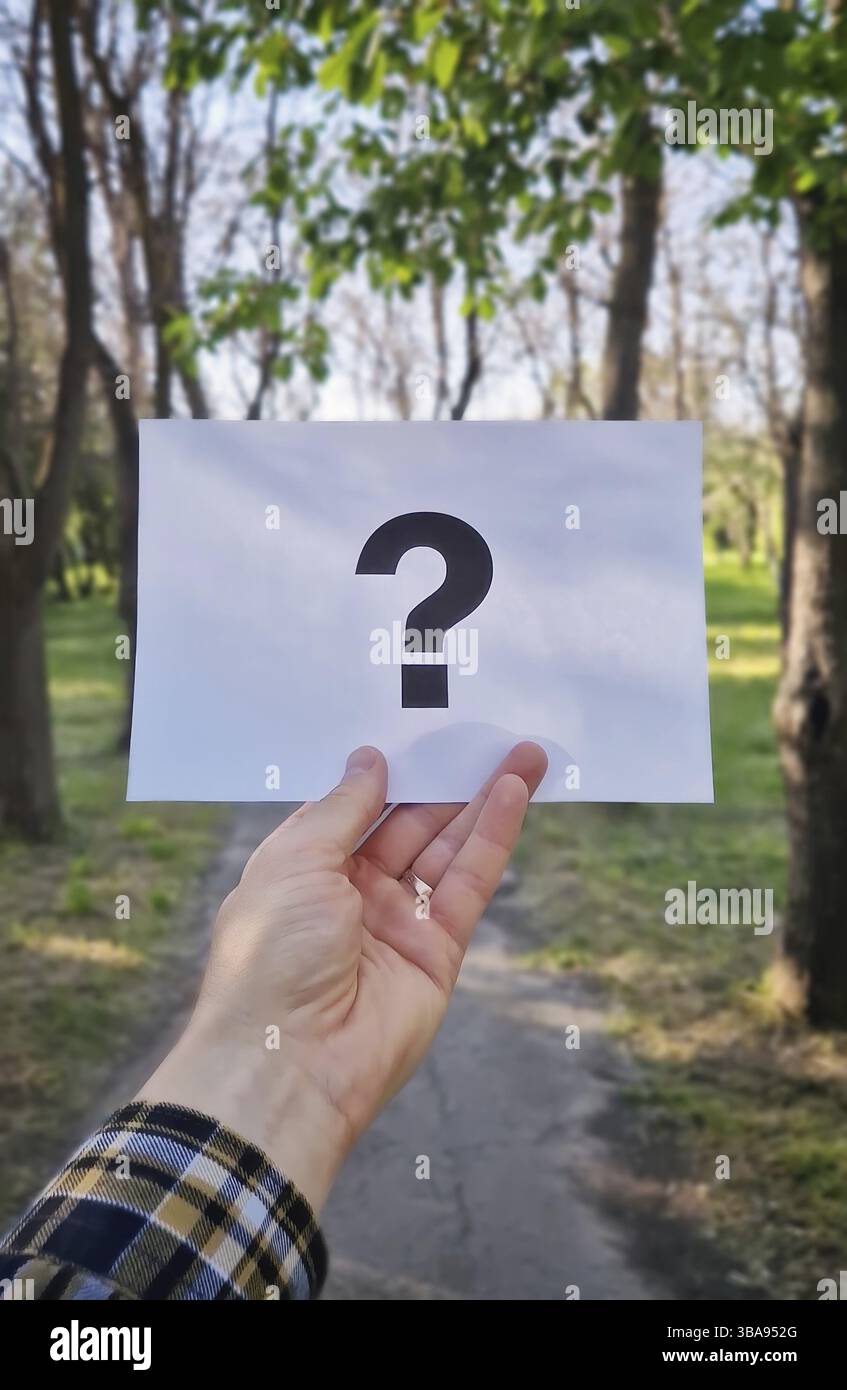 Male hand holding a white sheet of paper with a question mark on a path ...