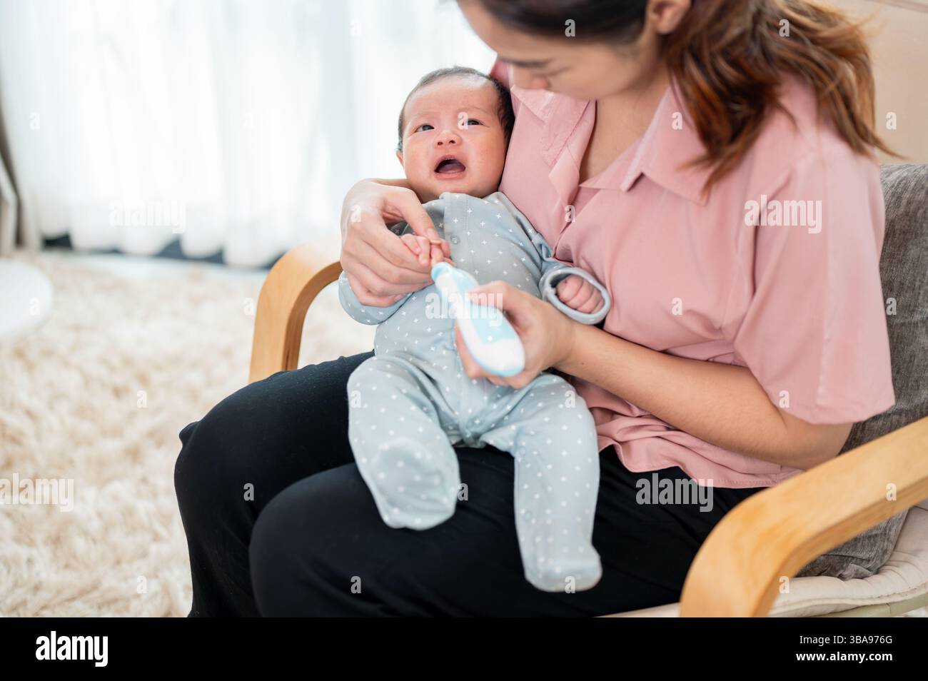 A caring Asian mom is trimming her newborn baby's nails on an armchair ...