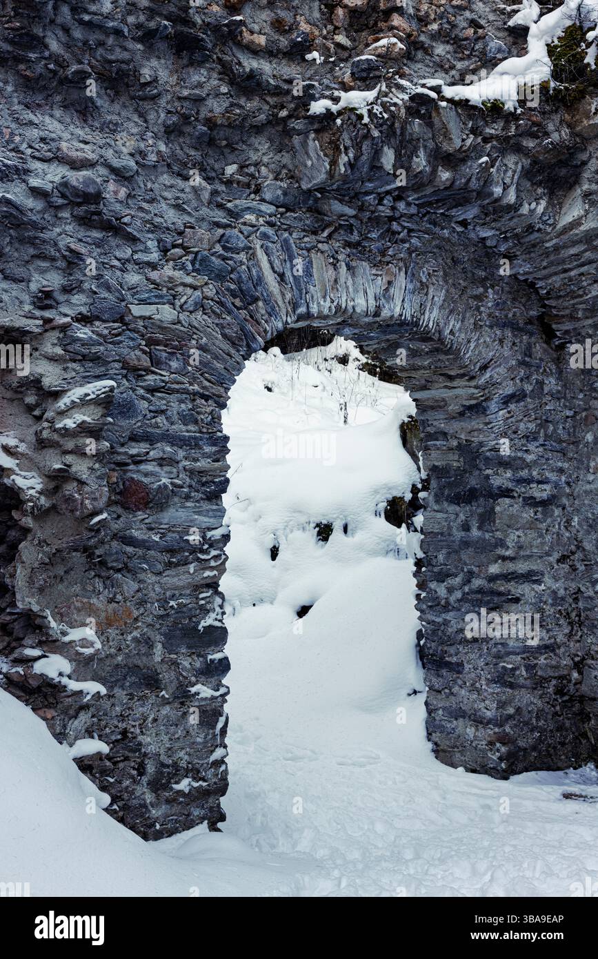 A narrow stone arch stands in deep snow, leading through ruined walls ...