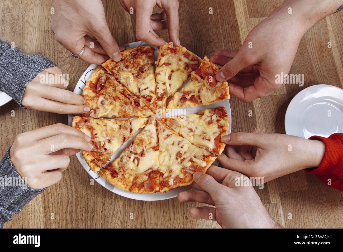 Group of hands grabbing pizza slices from a plate Stock Photo - Alamy