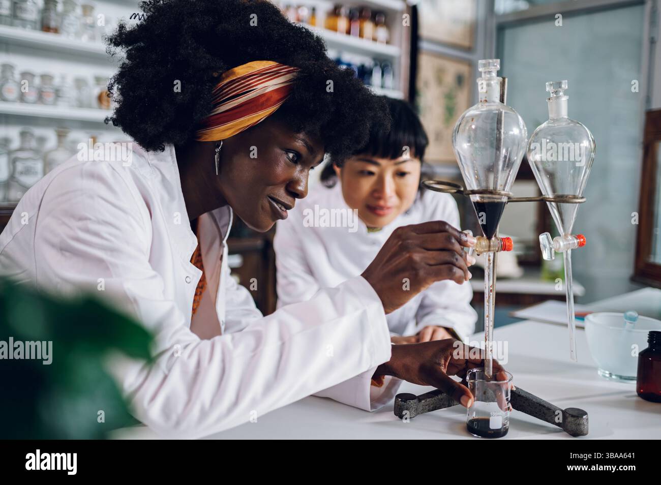 An interracial chemist is using a funnel in a vintage apothecary while ...