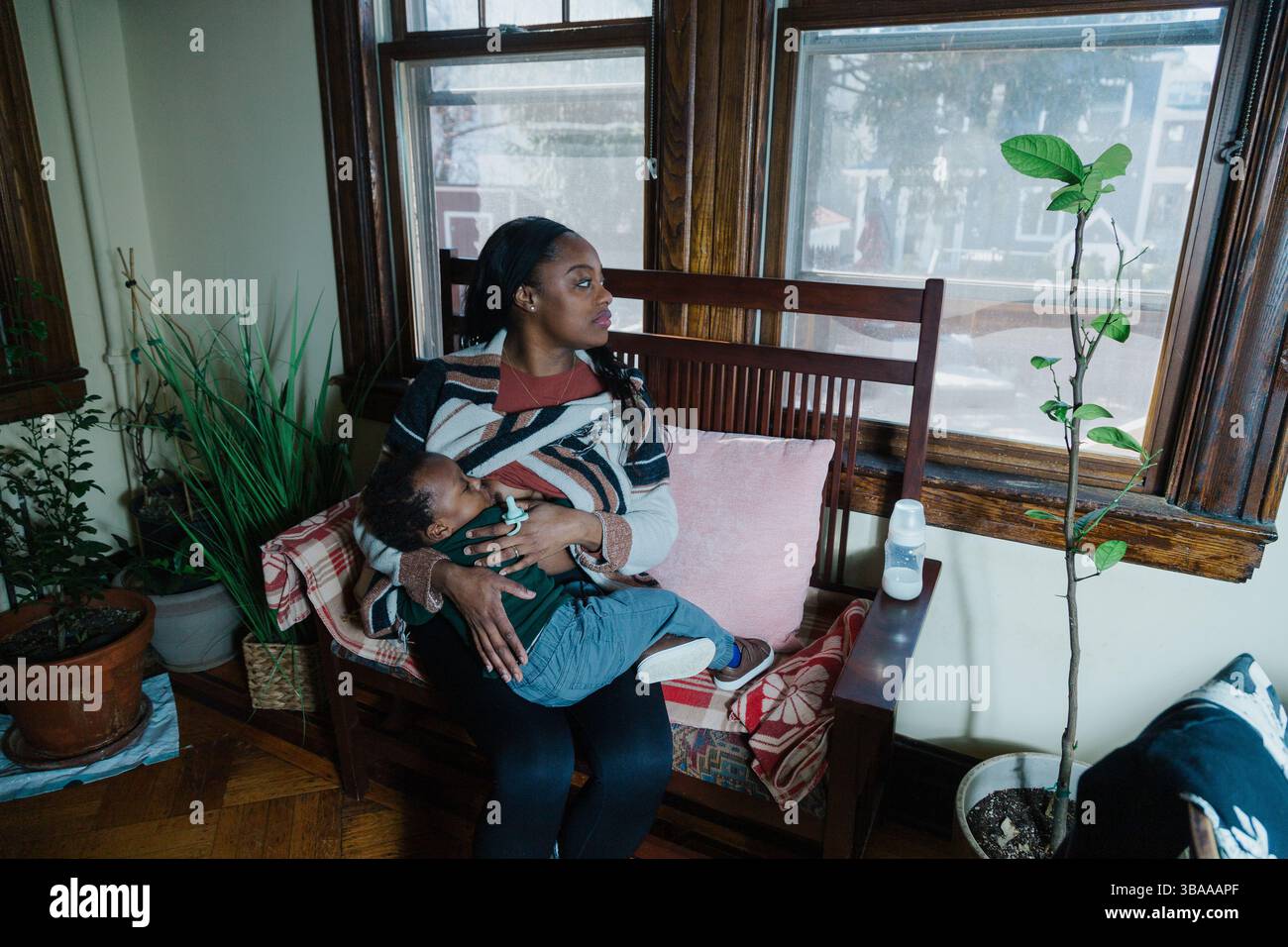 Baby with eyes closed latched onto mother holding pacifier sitting on ...
