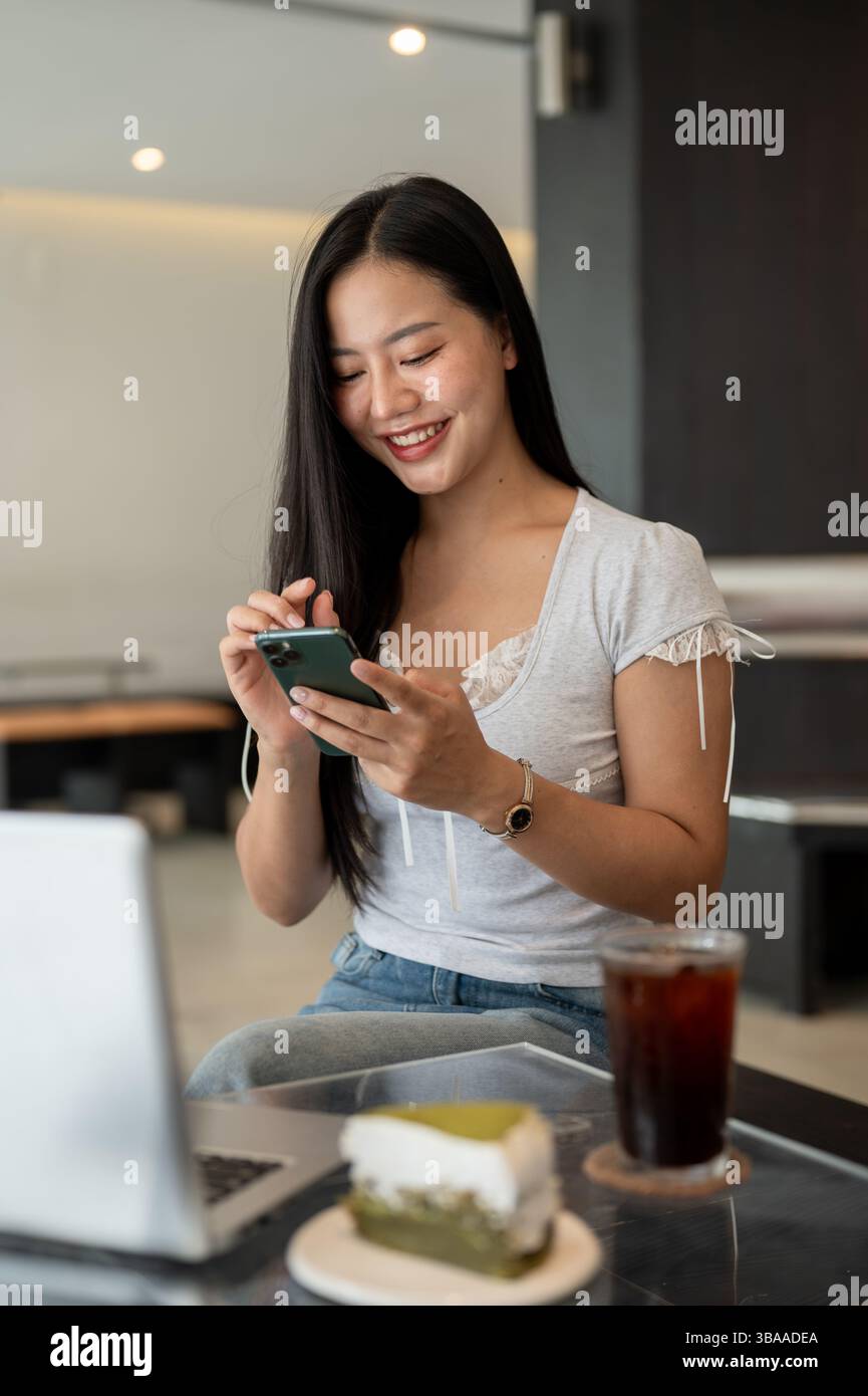 A beautiful, positive Asian woman using her smartphone while sitting in a modern coffee shop ...