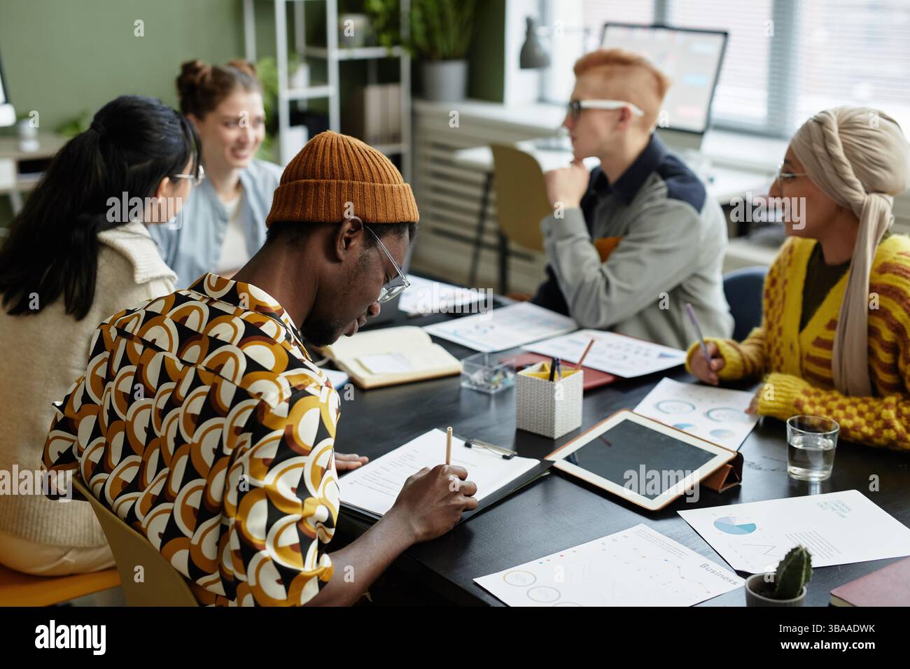 Back view at young black man taking notes in meeting with creative ...