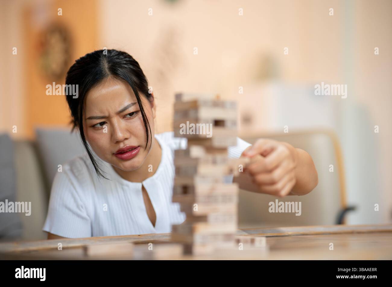 A beautiful, focused Asian woman carefully moves a wooden block to ...