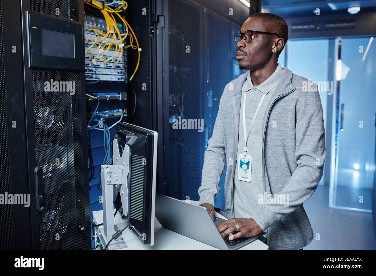 Waist up portrait of adult black man working as IT engineer using laptop while setting up ...