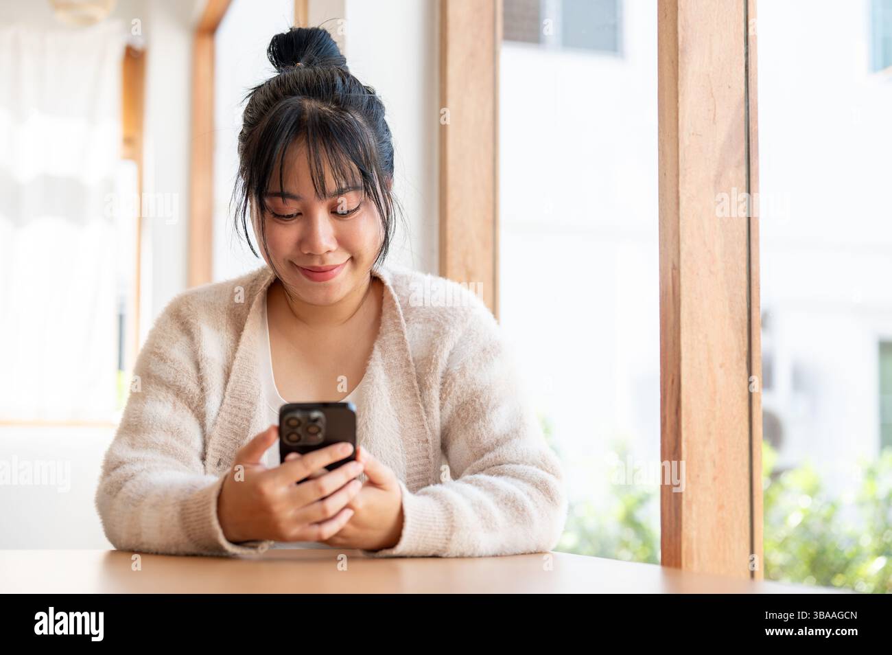 A happy young Asian woman responding to messages on her smartphone ...