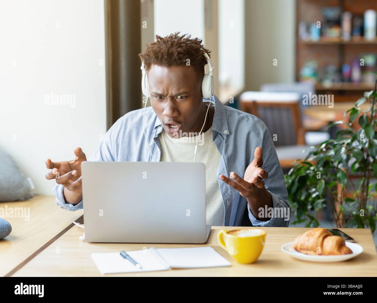 Stressed African American guy in headphones using laptop to work on ...