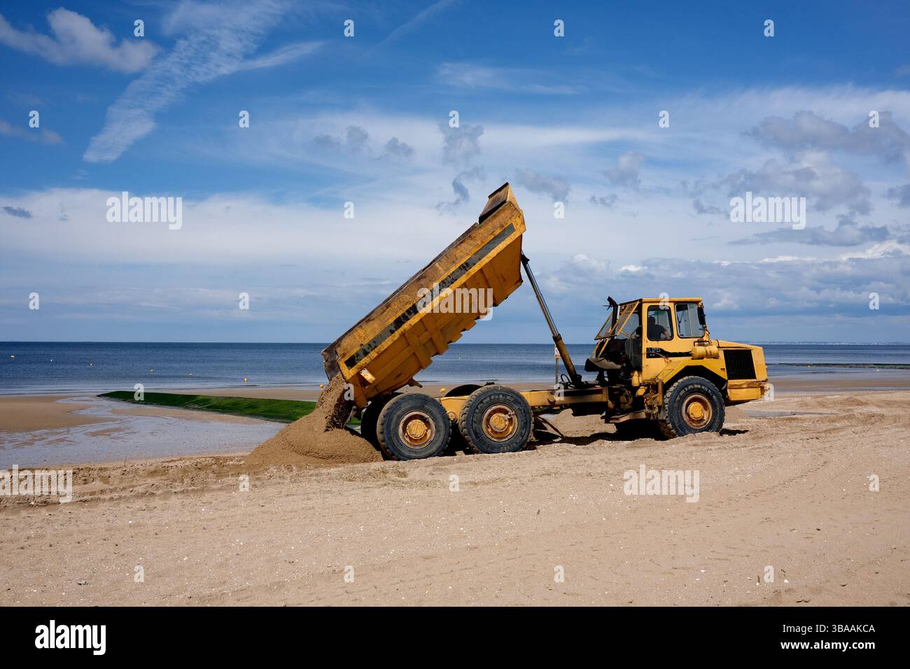Municipal workers using heavy mechanical tractors redistributing sand ...