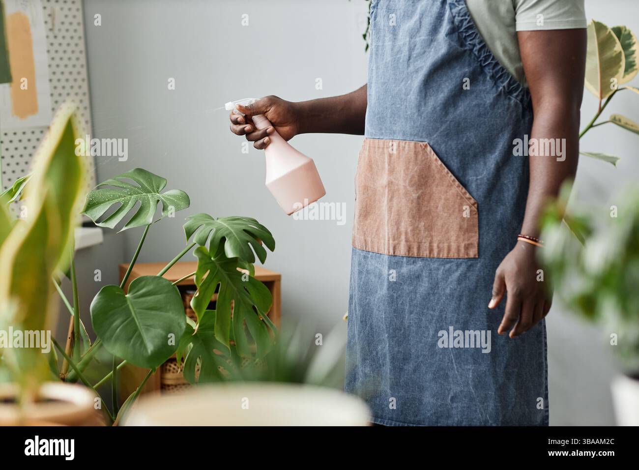Side view close up of unrecognizable black man watering plants indoors ...