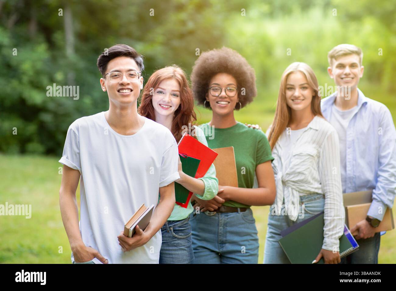 Diverse group of students holding workbooks standing together on ...