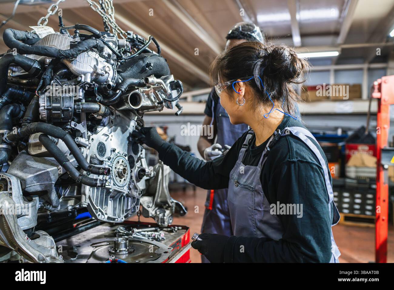 Female and male mechanics working together on a car engine suspended by ...