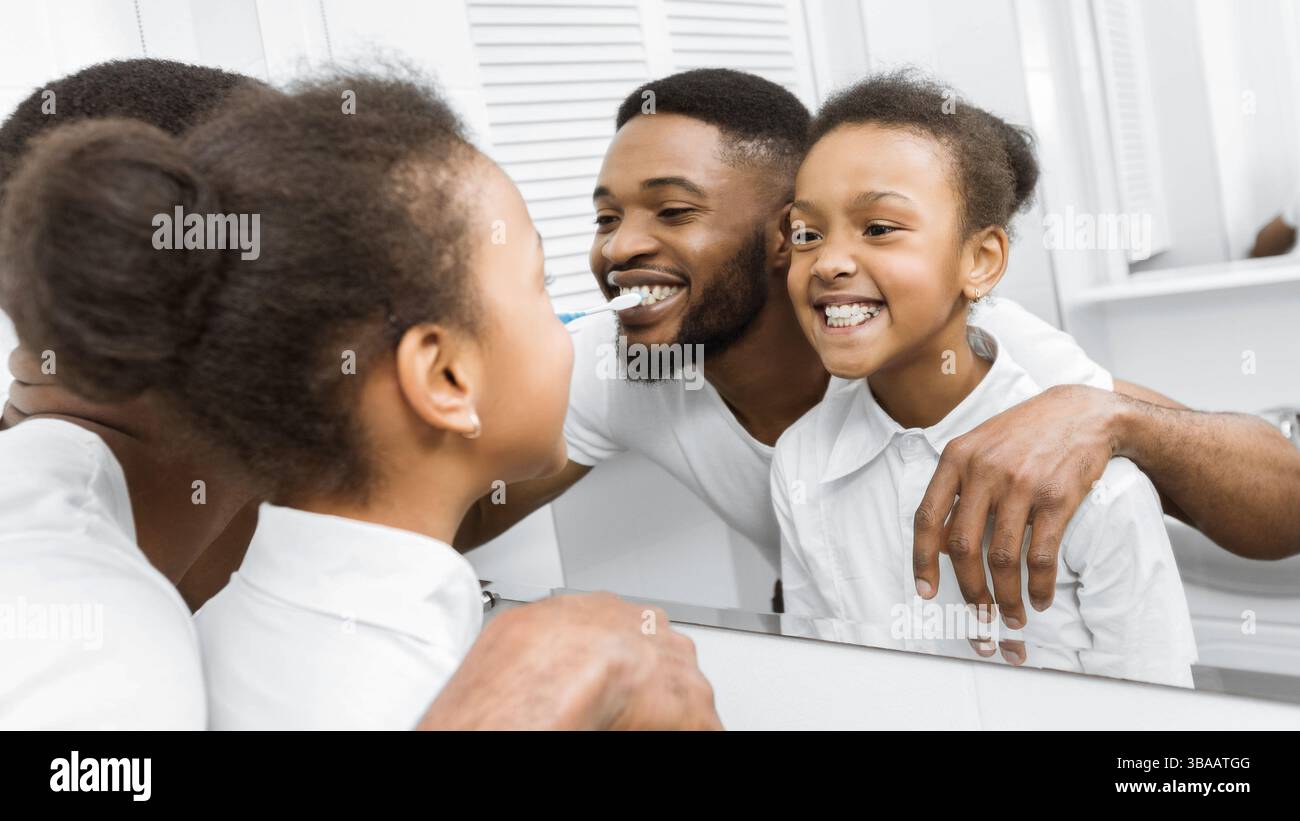 Morning routine. Afro girl and father brushing teeth together , looking at mirror, panorama ...