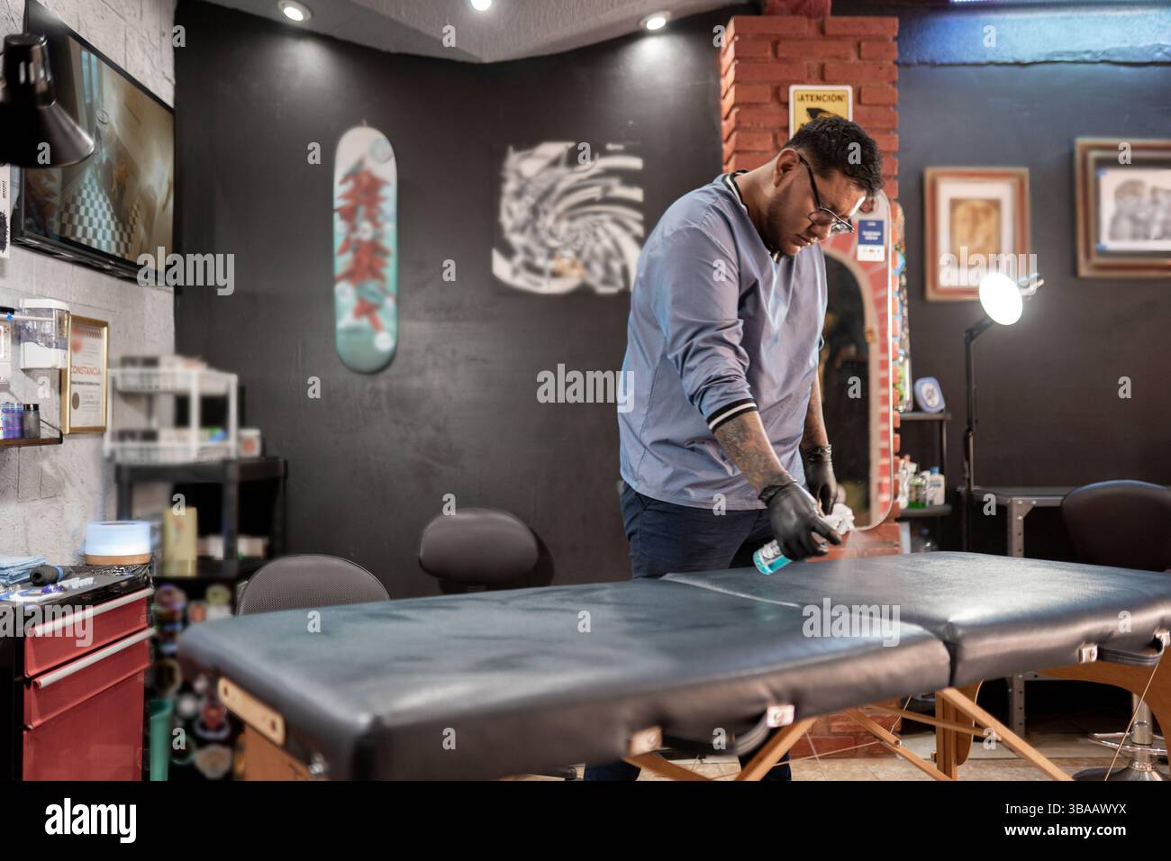 A tattoo artist is cleaning the studio stretcher with a spray. Concept ...