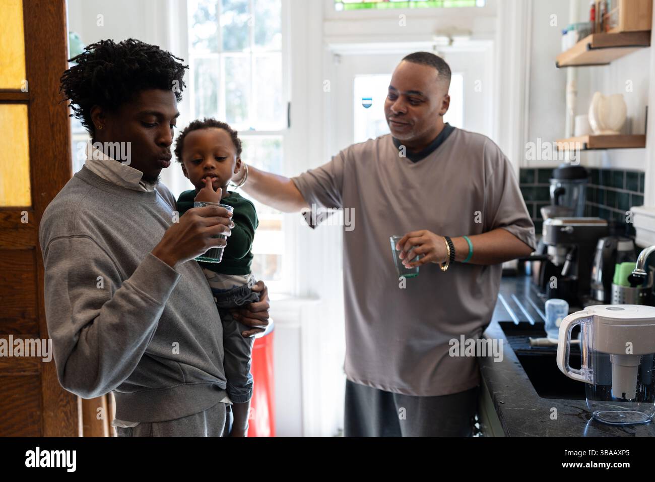 Black dad holding son with glass of water in hand standing in kitchen ...