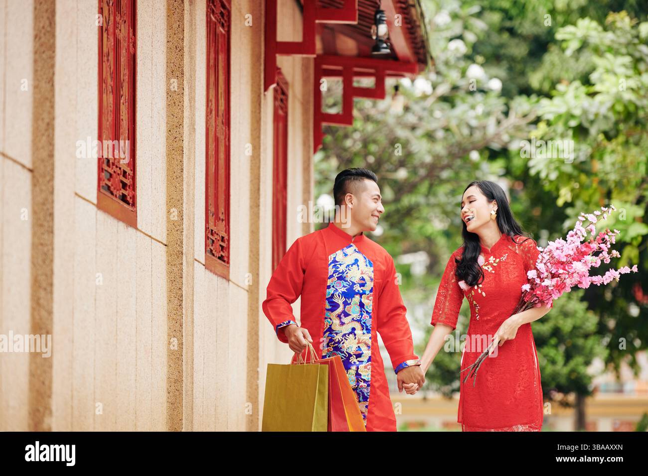 Happy young Asian couple holding hands when walking outdoors in traditional clothing with ...
