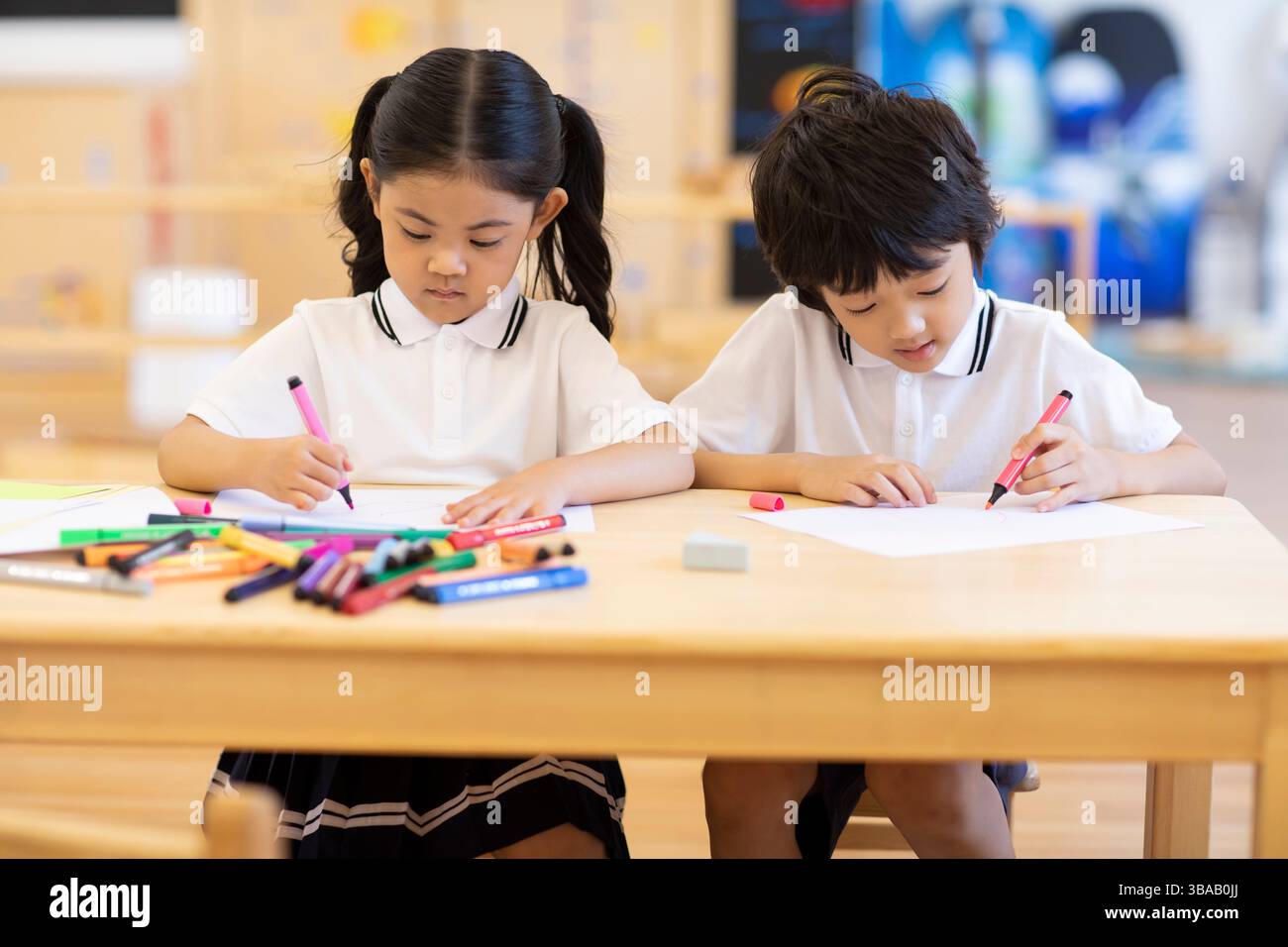 Chinese children drawing using crayons sitting at table in classroom ...