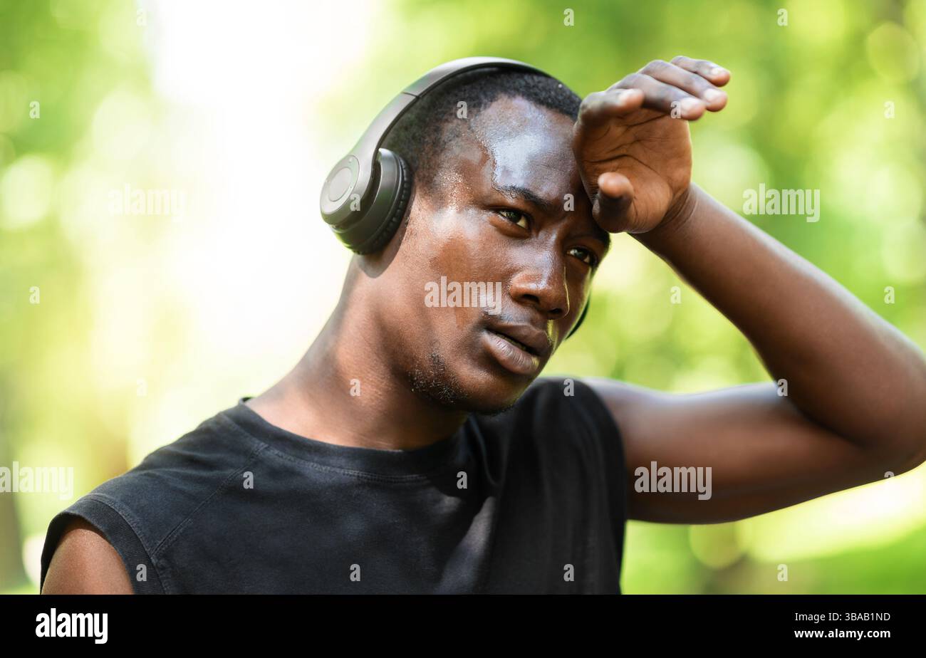 Exhausted black guy training at public park, listening to music with ...