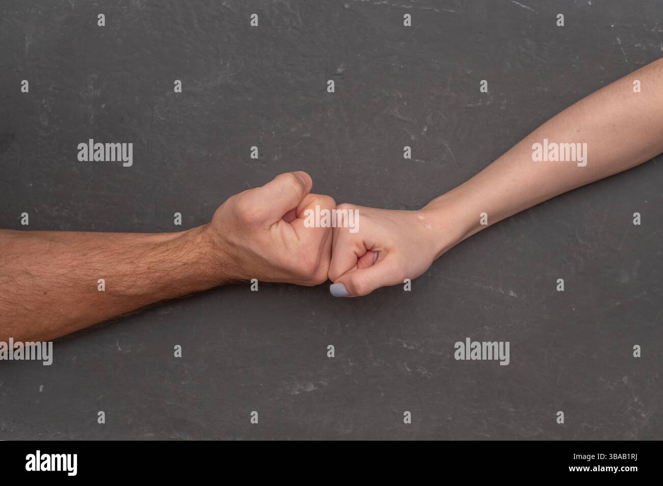 Male fist pressing against female fist on gray background, intense ...