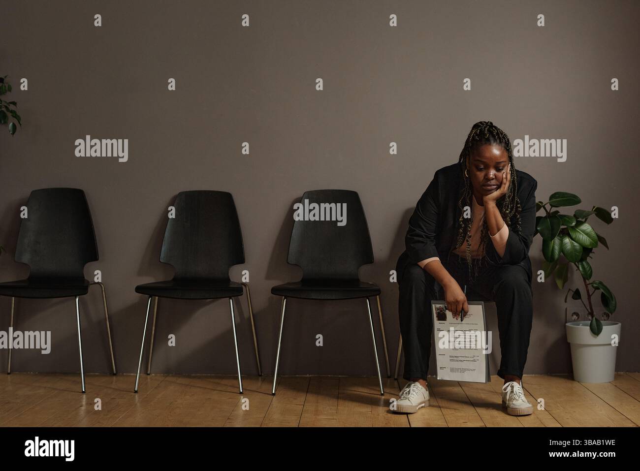 Serious Black woman leaning face on hand holding resume sitting on ...