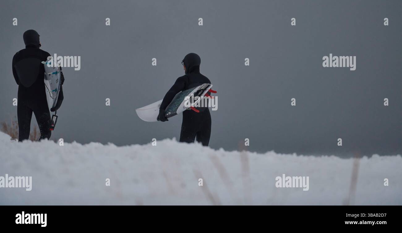 Authentic local Arctic surfers running on snowy beach after surfing in ...