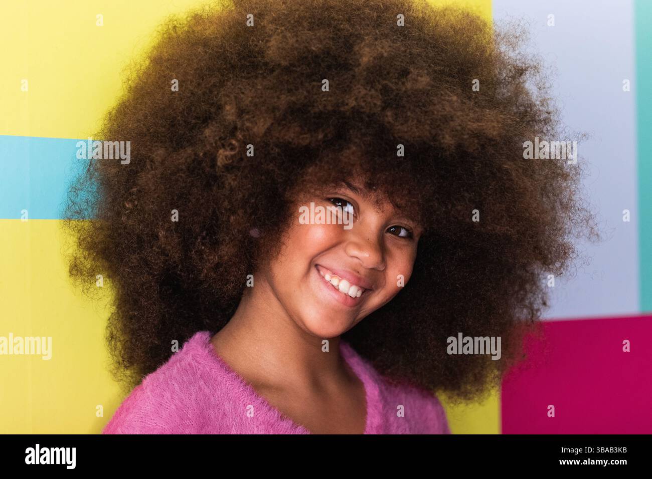 Mixed-race girl with afro standing against colorful wall in studio ...
