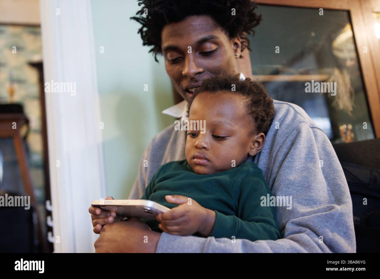 Black boy watching on smartphone while sitting on the father's lap in ...