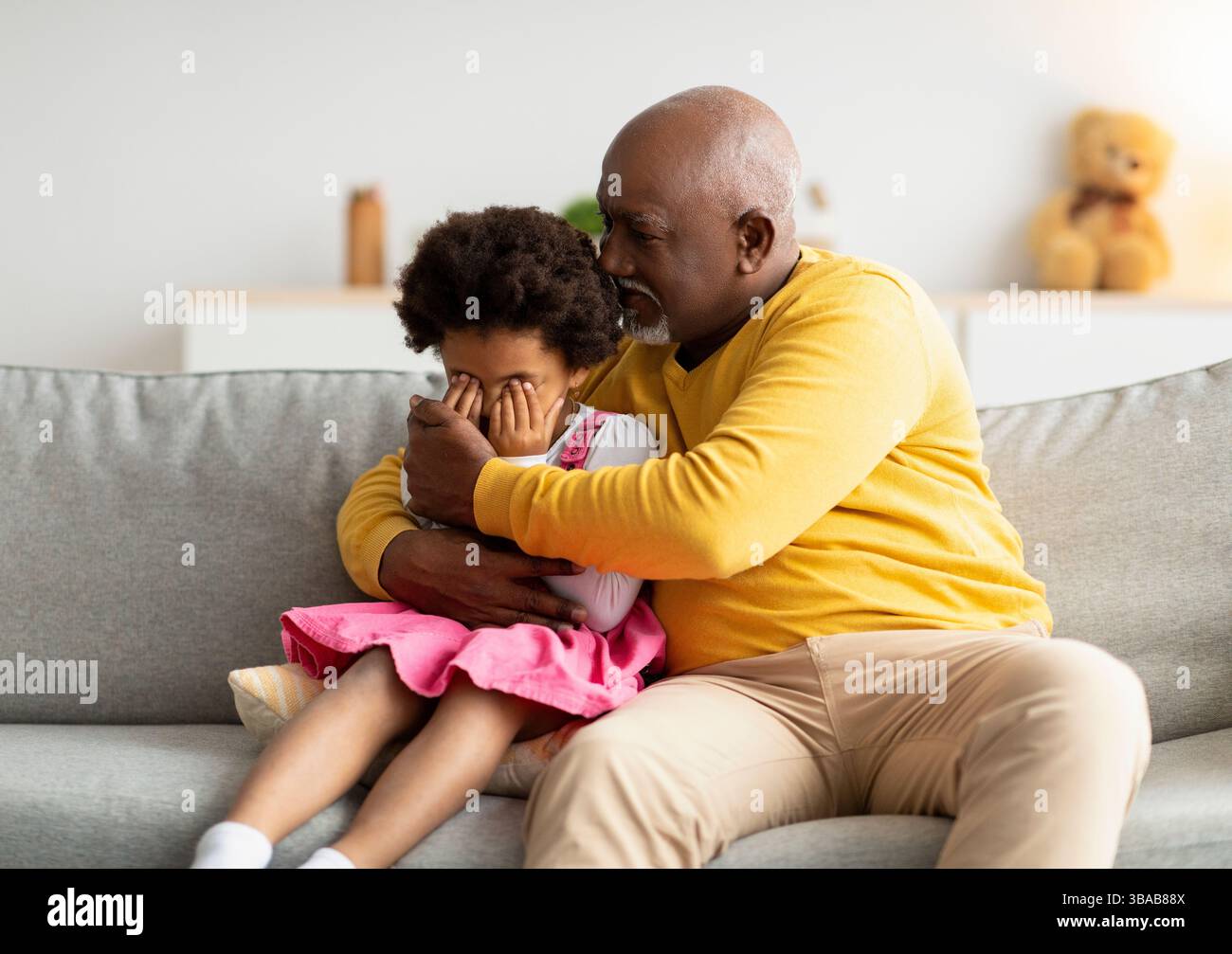 Black elderly man calming upset sad crying little girl in living room ...