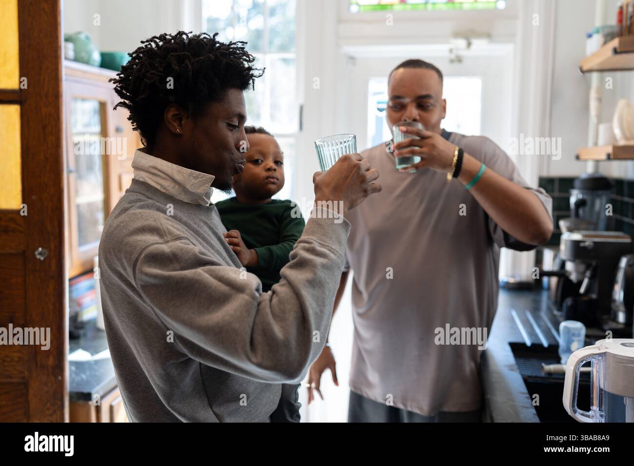 Black dad holding son drinking glass of water standing in kitchen with ...