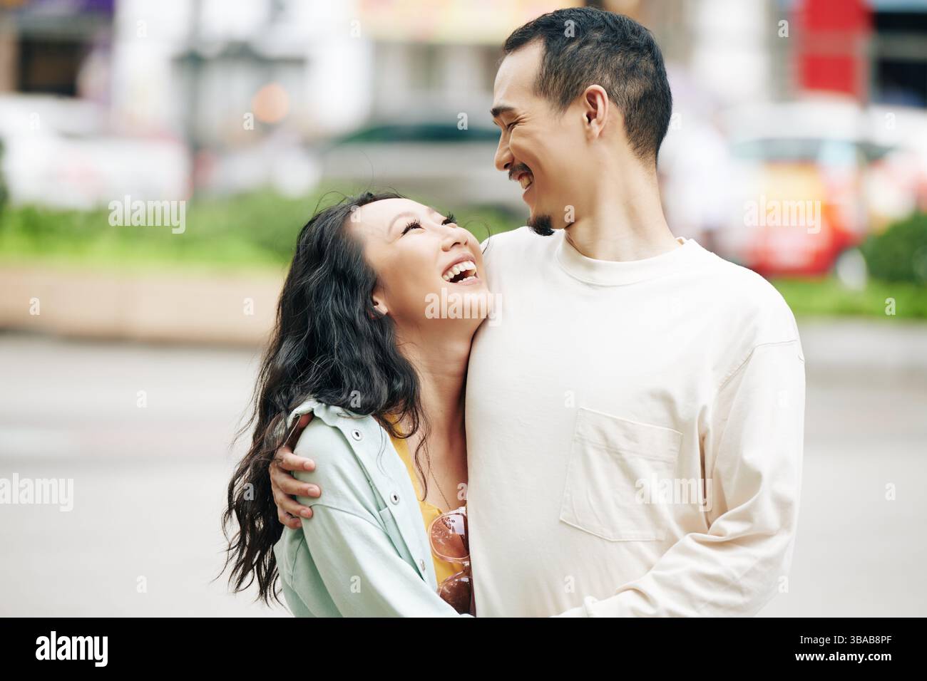 Happy young Chinese boyfriend and girlfriend laughing and looking at ...