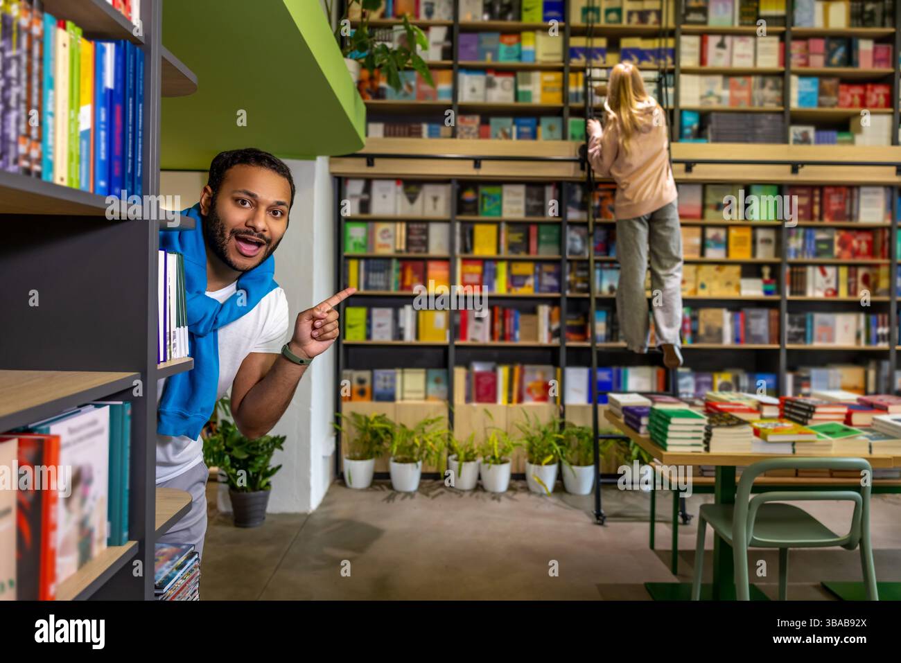 In the library. Young dark-skinned man hiding behind the bookshelves ...