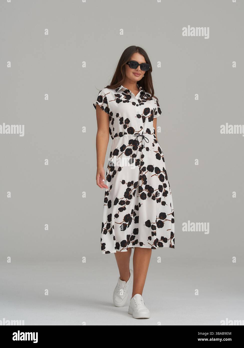 Woman in a white floral dress walking confidently, wearing sunglasses ...