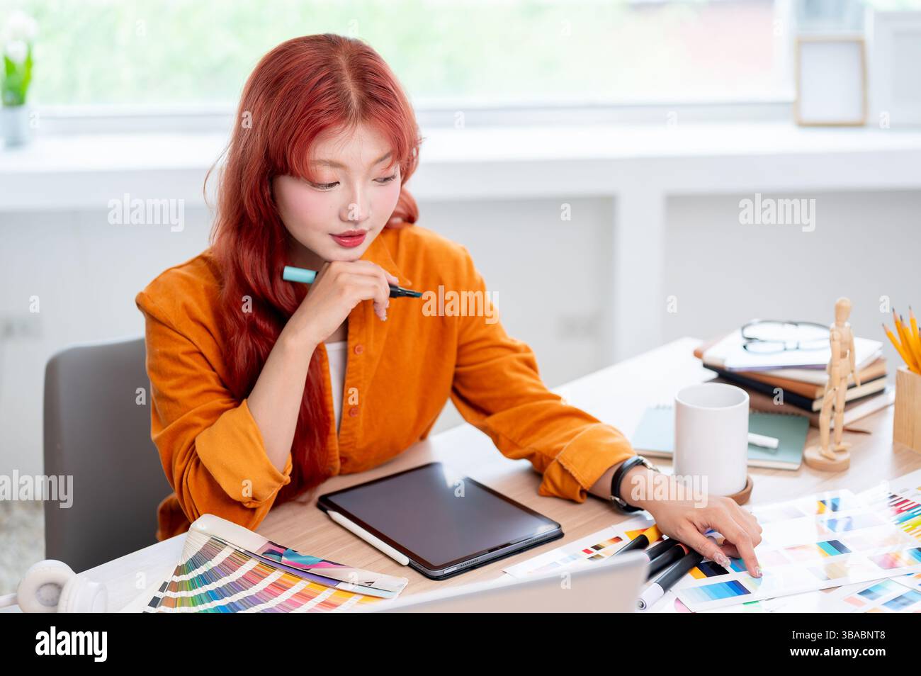 A creative and focused Asian female graphic designer with red hair is ...