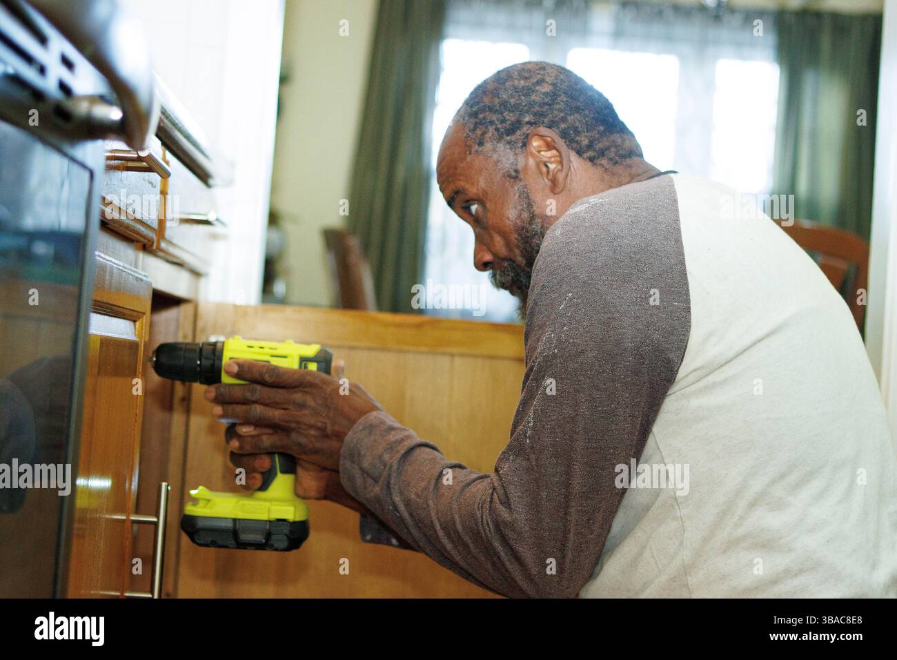 Senior Black man fixing cabinet door using screwdriver crouching on ...
