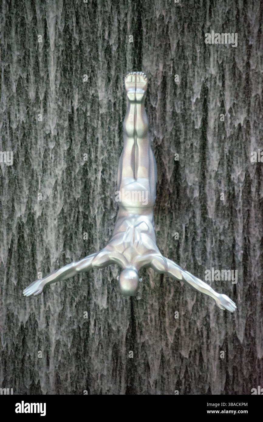 A silver sculpture of a diver in a vertical position, poised above a ...