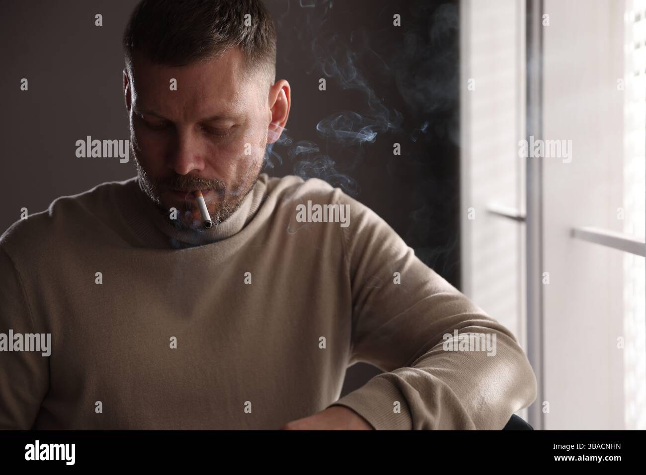 Man smoking cigarette near window in room Stock Photo - Alamy