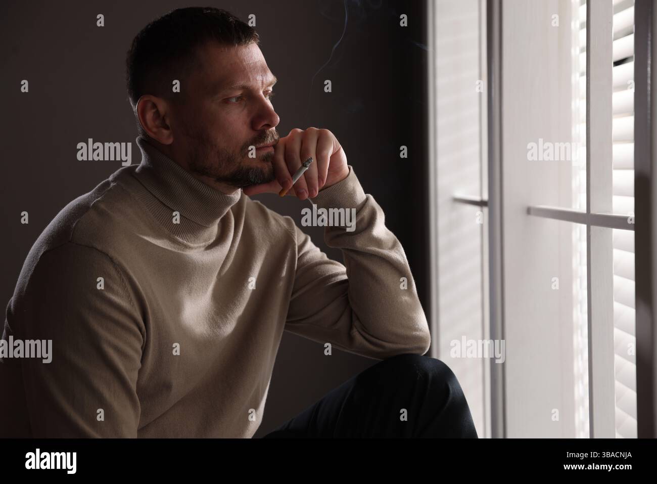 Man smoking cigarette near window in room Stock Photo - Alamy
