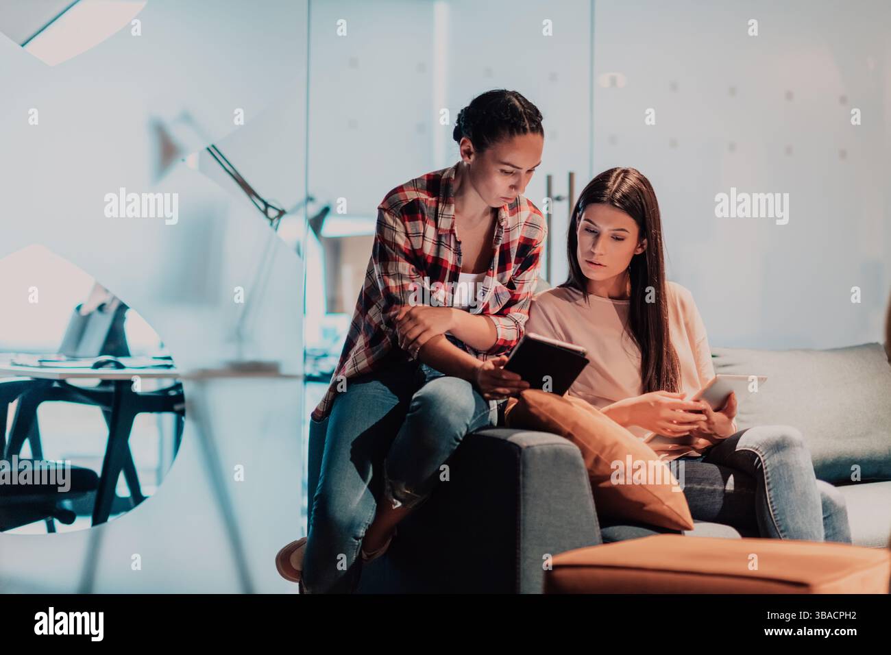 Two young women in a modern office solve a problem together while using ...