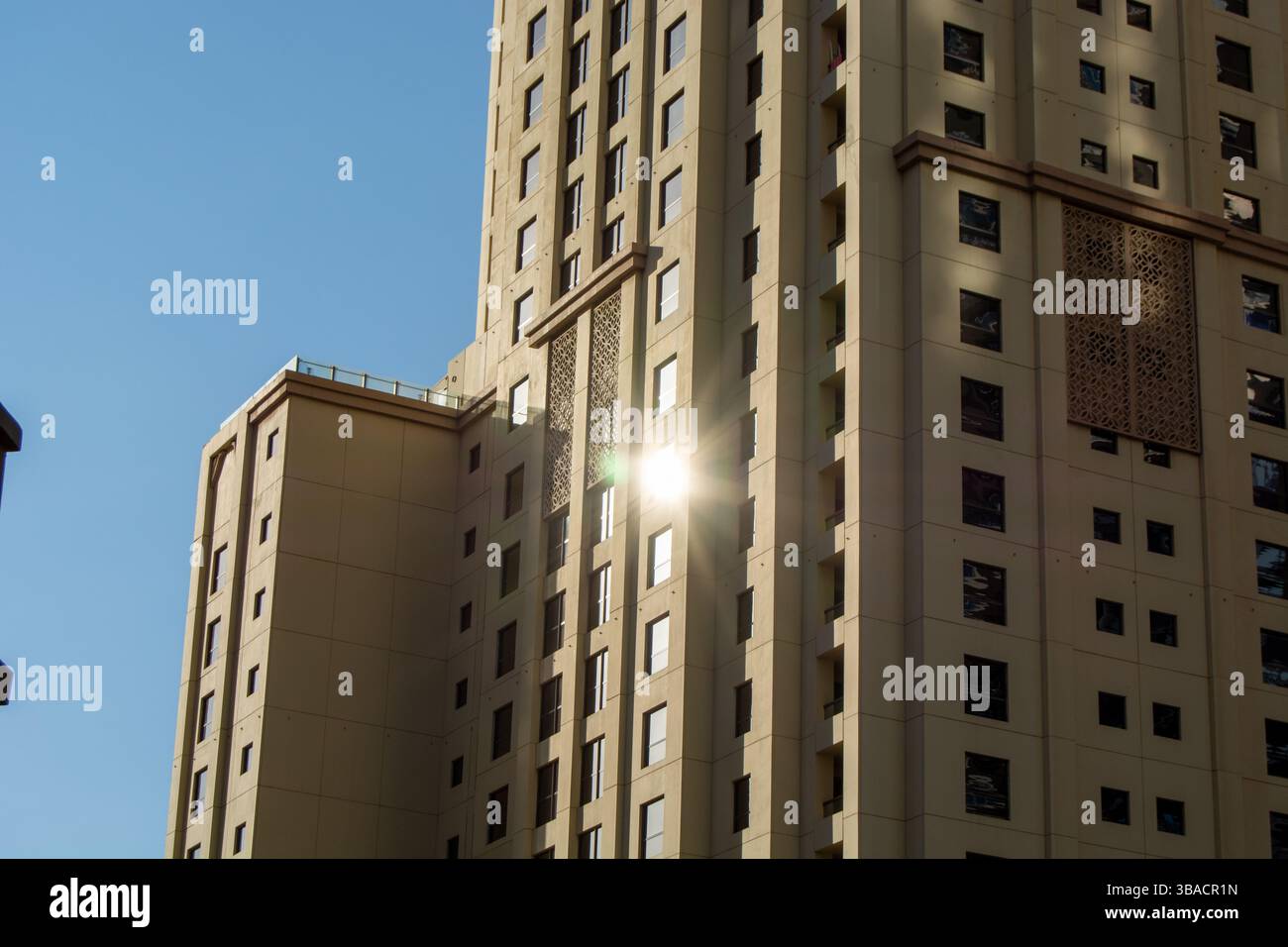 A tall, modern building with a reflective surface catching sunlight ...