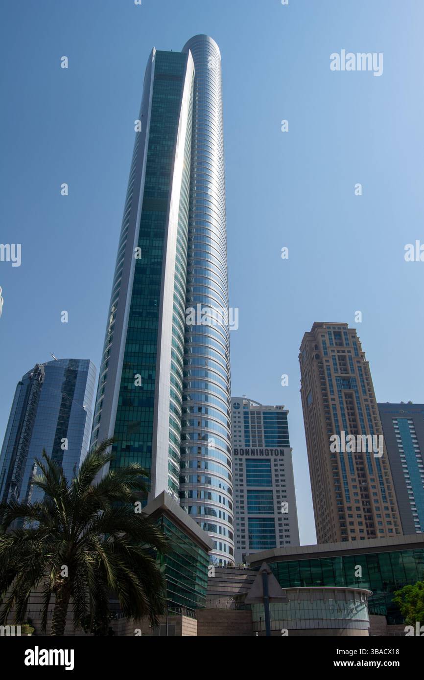 A tall modern skyscraper with a sleek glass facade, surrounded by other buildings and palm trees ...