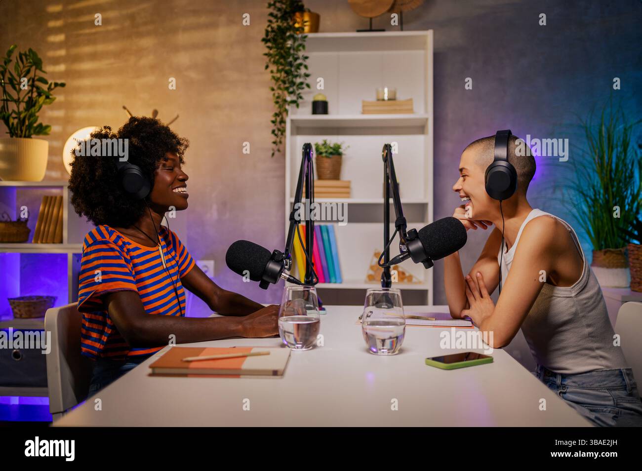 Two cheerful multiracial gen z girls are sitting in a home recording ...